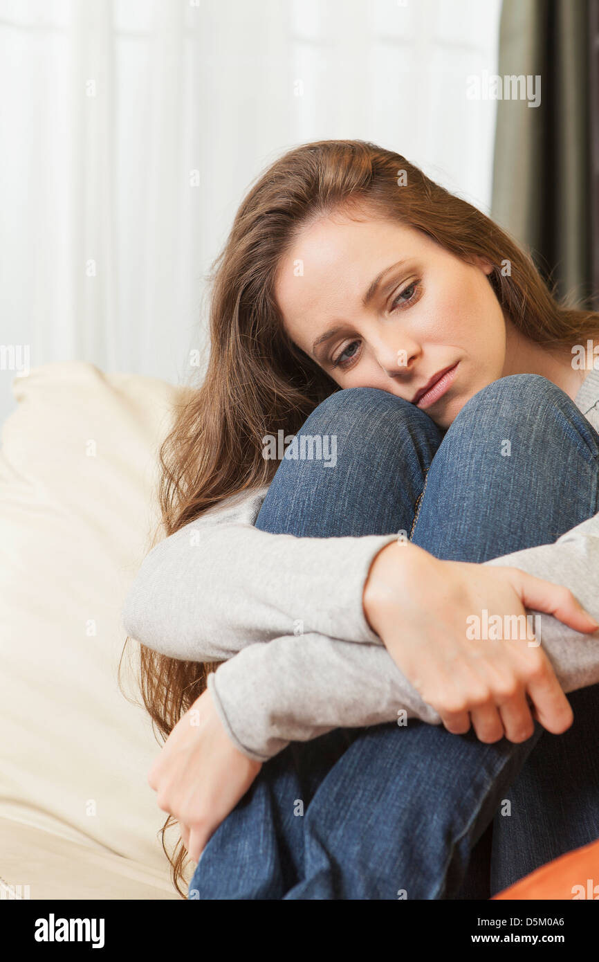Sad woman sitting on sofa and looking away Stock Photo - Alamy