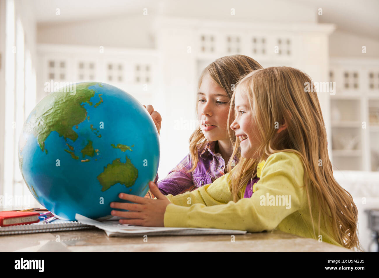 Two girls (6-7) doing homework with globe Stock Photo - Alamy