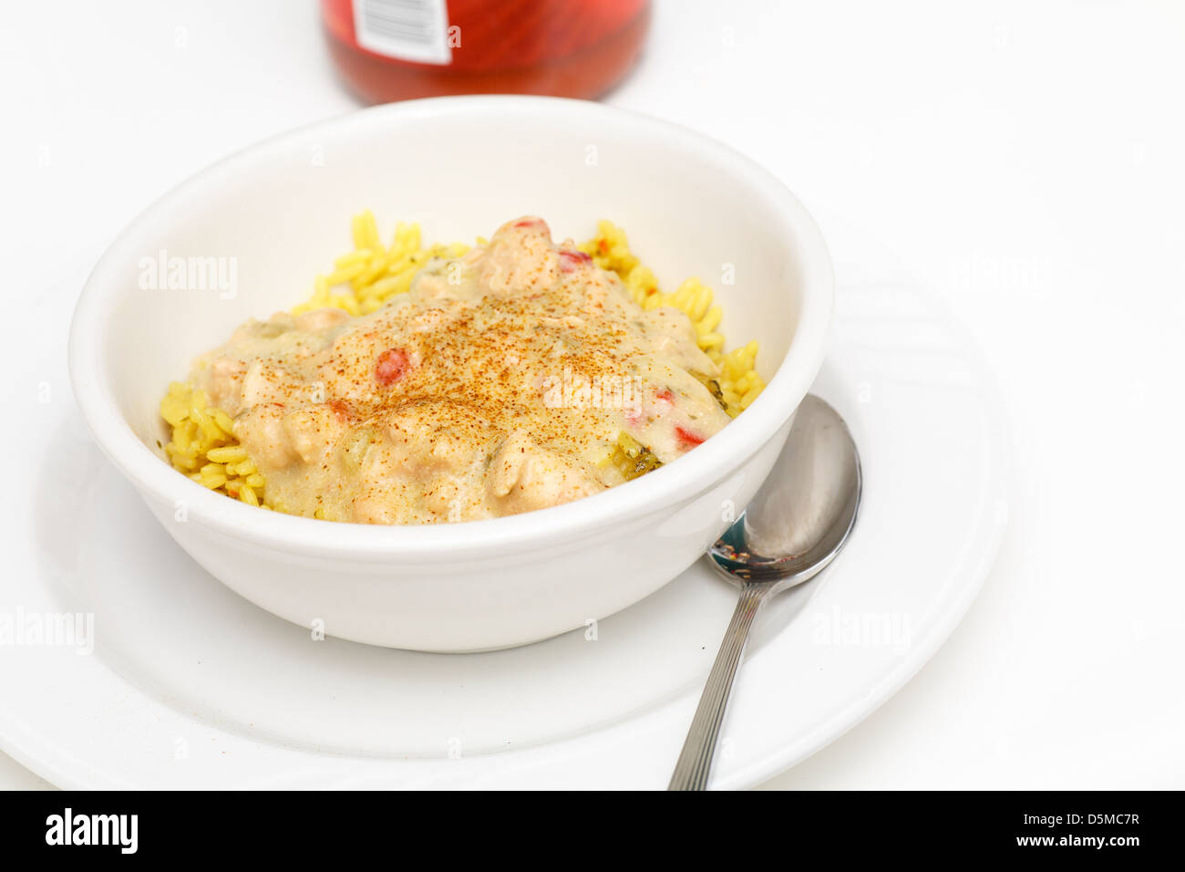 A white bowl of chicken chili over yellow rice garnished with cayenne ...