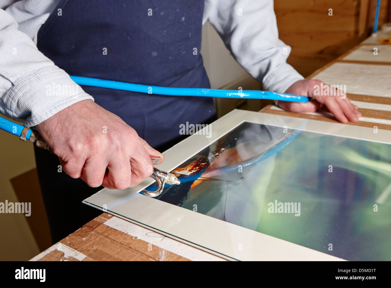 framer using air line to clean dust off a frame in a framing workshop ...