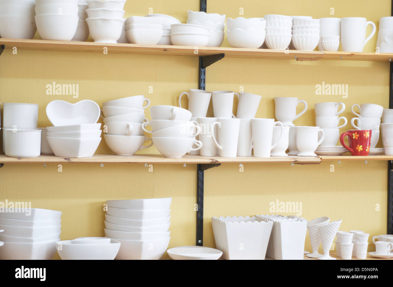 Three shelves of unfinished pottery except for one finished coffee mug ...