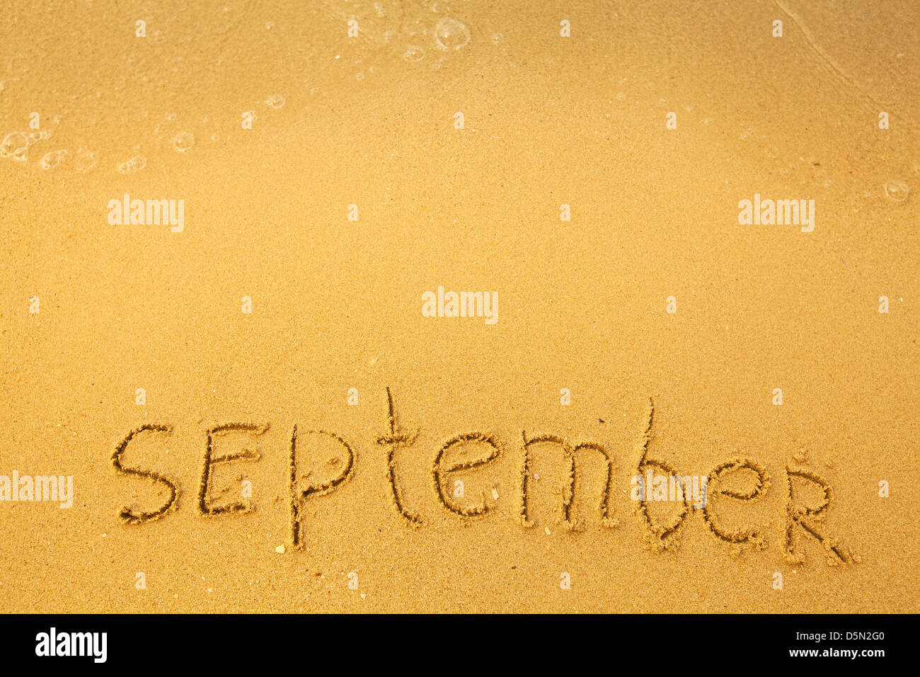 September - written in sand on beach texture - soft wave of the sea ...