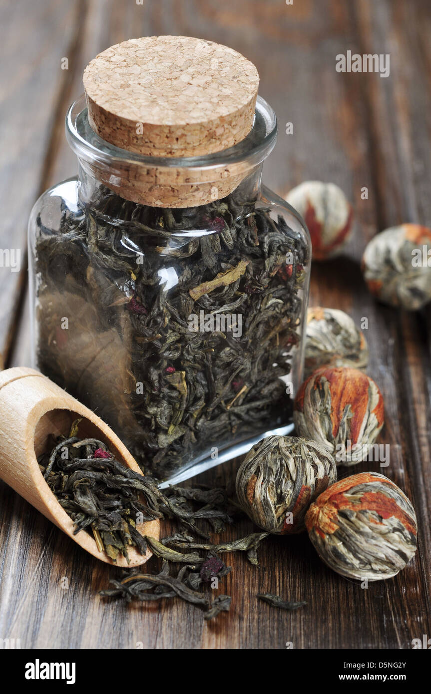 Green tea balls with flowers and glass jar with tea on wooden table ...