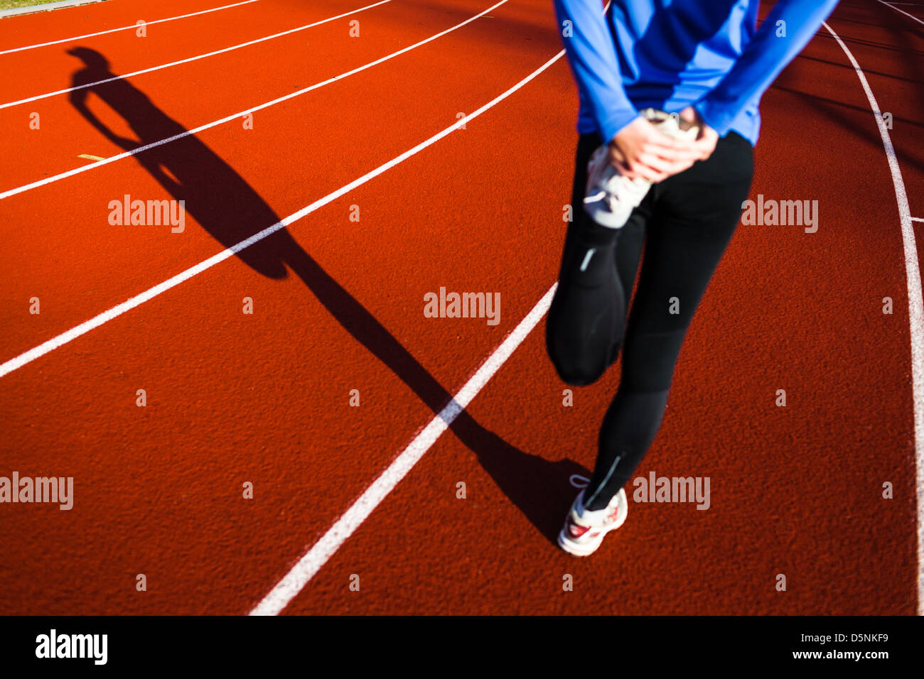 Young woman stretching before her run casts a shadow on the track Stock ...