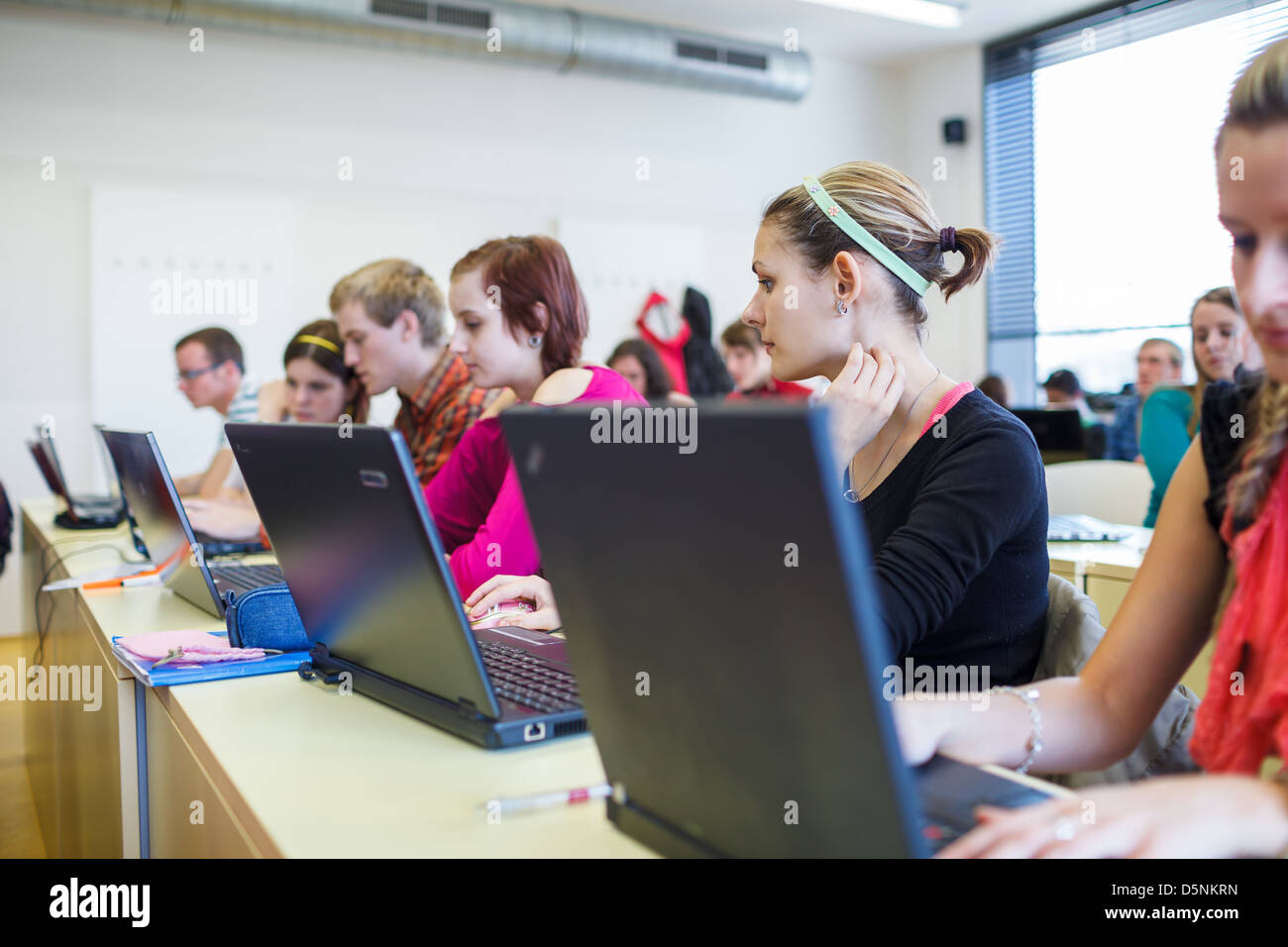 College students sitting in a classroom, using laptop computers during ...