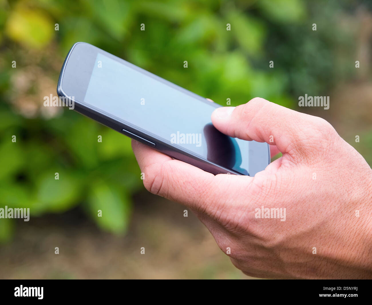 Man hand touching screen on modern mobile smart phone on natural green ...