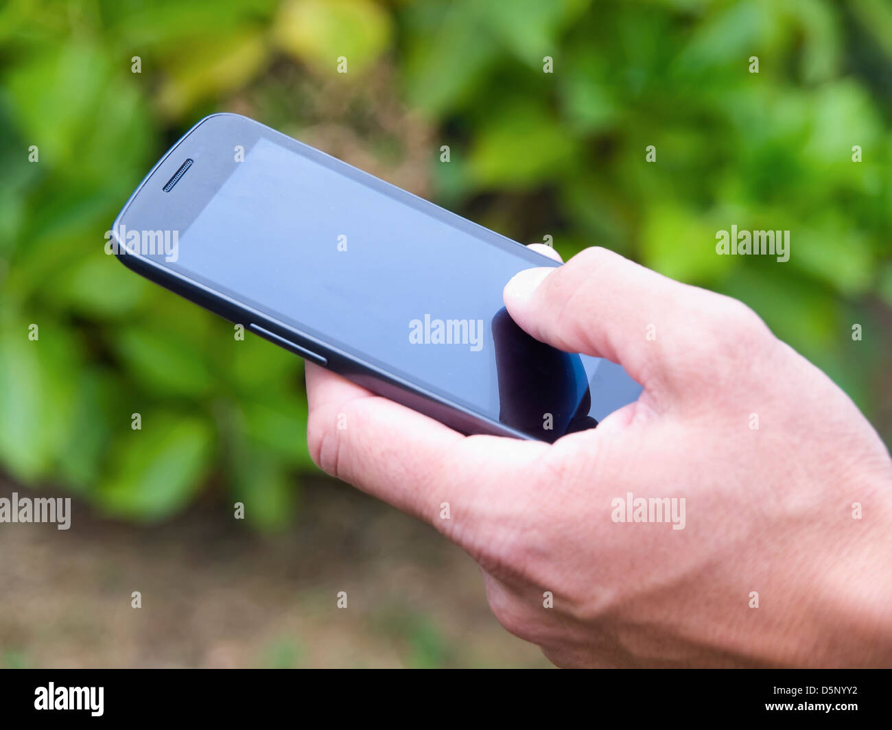 Man hand touching screen on modern mobile smart phone on natural green ...