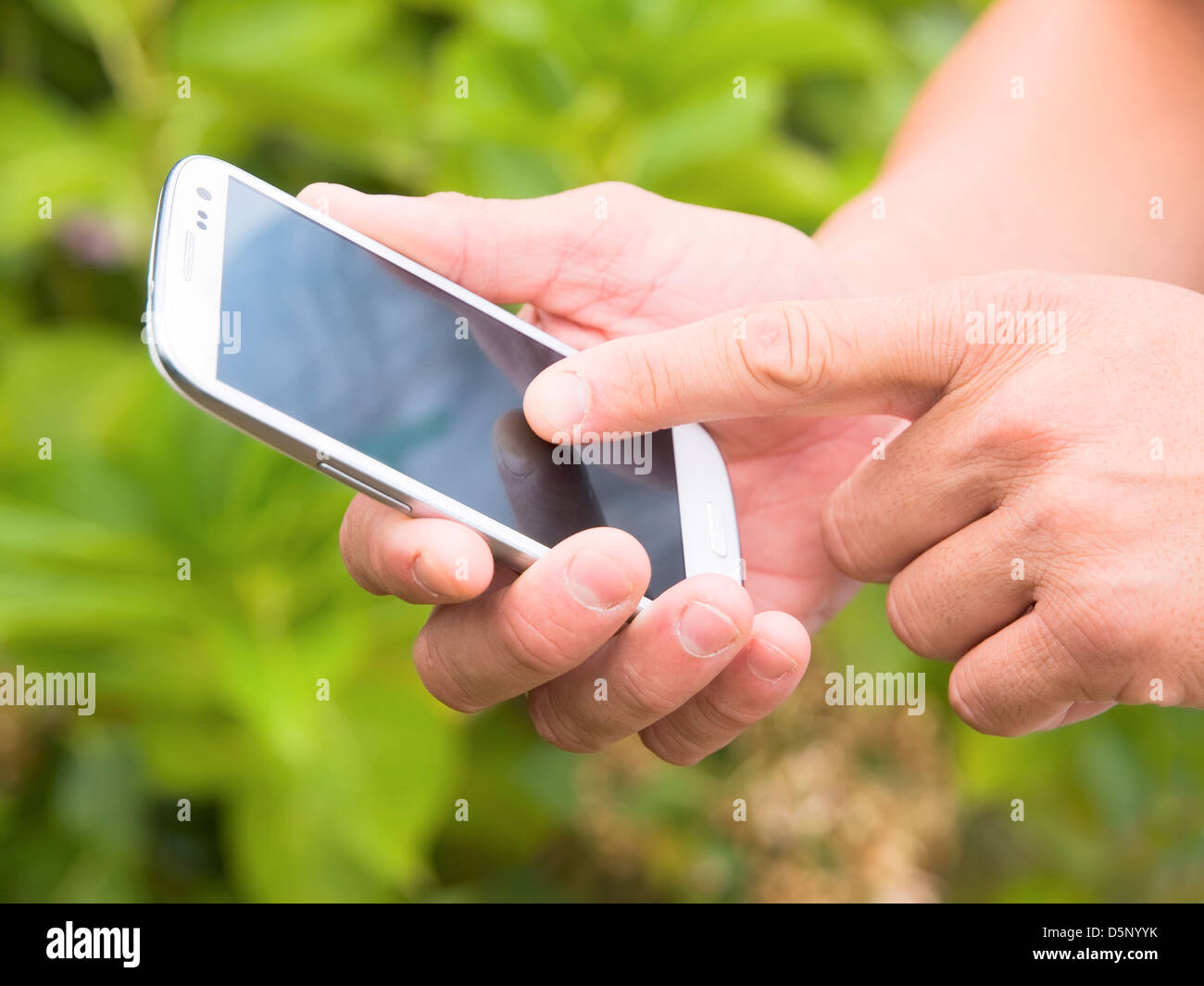 Man hand touching screen on modern mobile smart phone on natural green ...