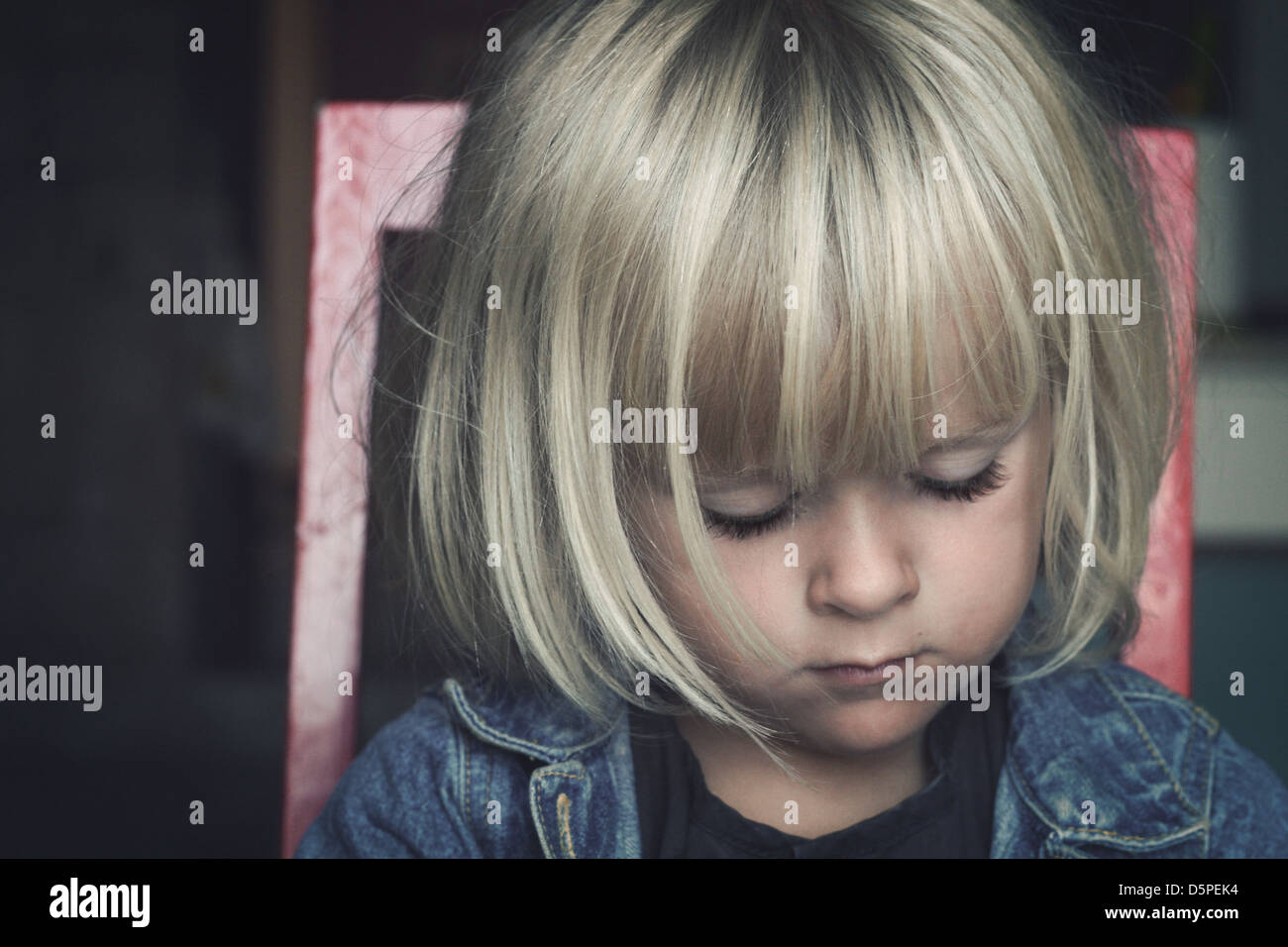 Sad little child sitting on a chair, looking down Stock Photo - Alamy
