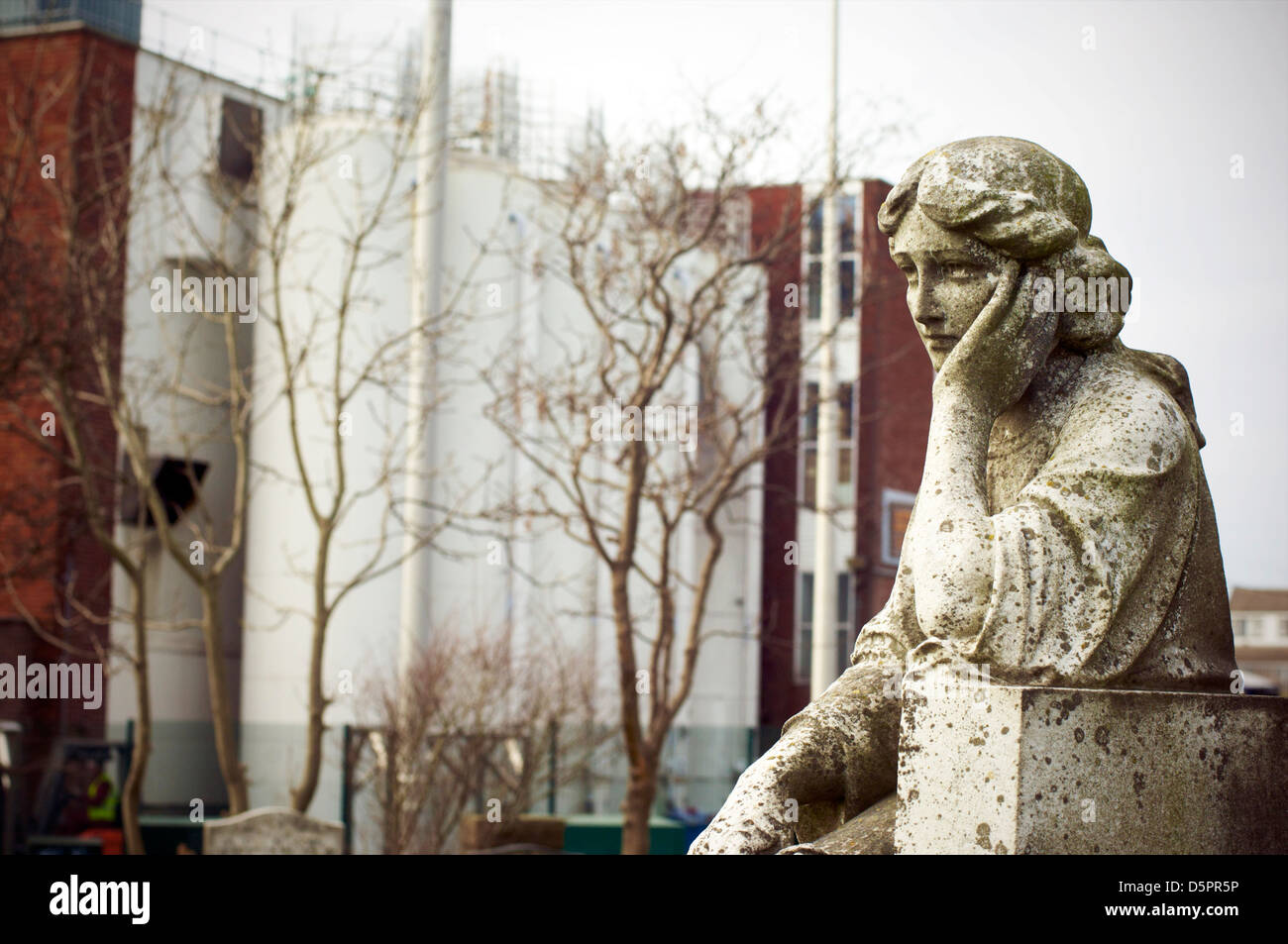 Stone statue of sad women on grave in cemetery with industrial backdrop ...