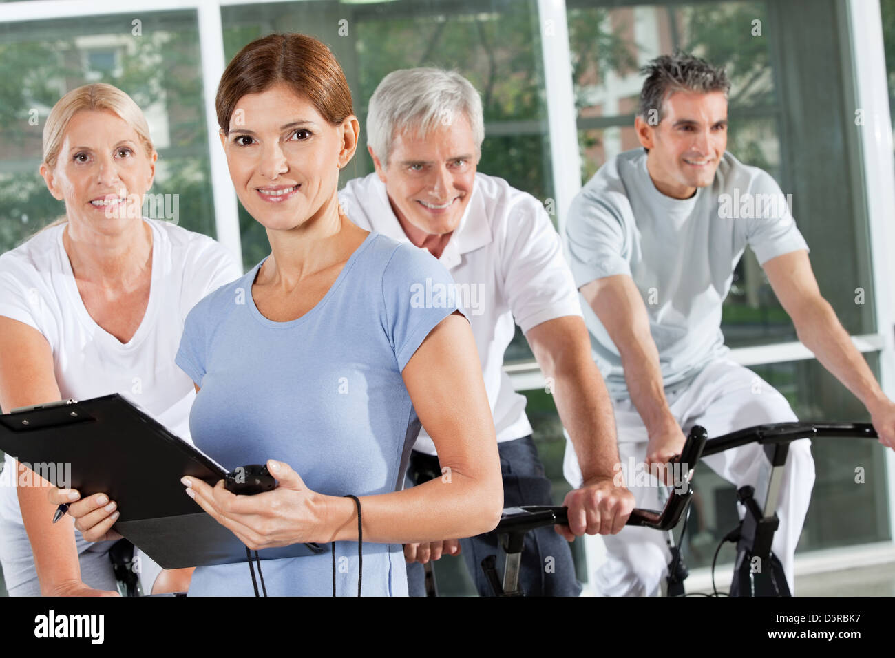 Fitness trainer coaching spinning exercise class with seniors in gym ...