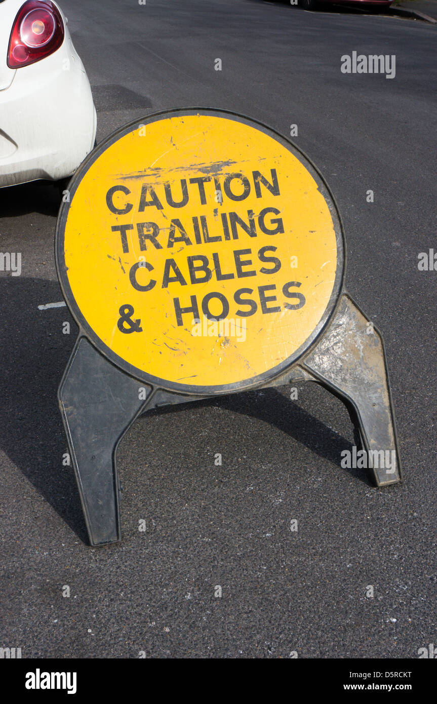 A sign warns of trailing cables and hoses before an area of road works ...