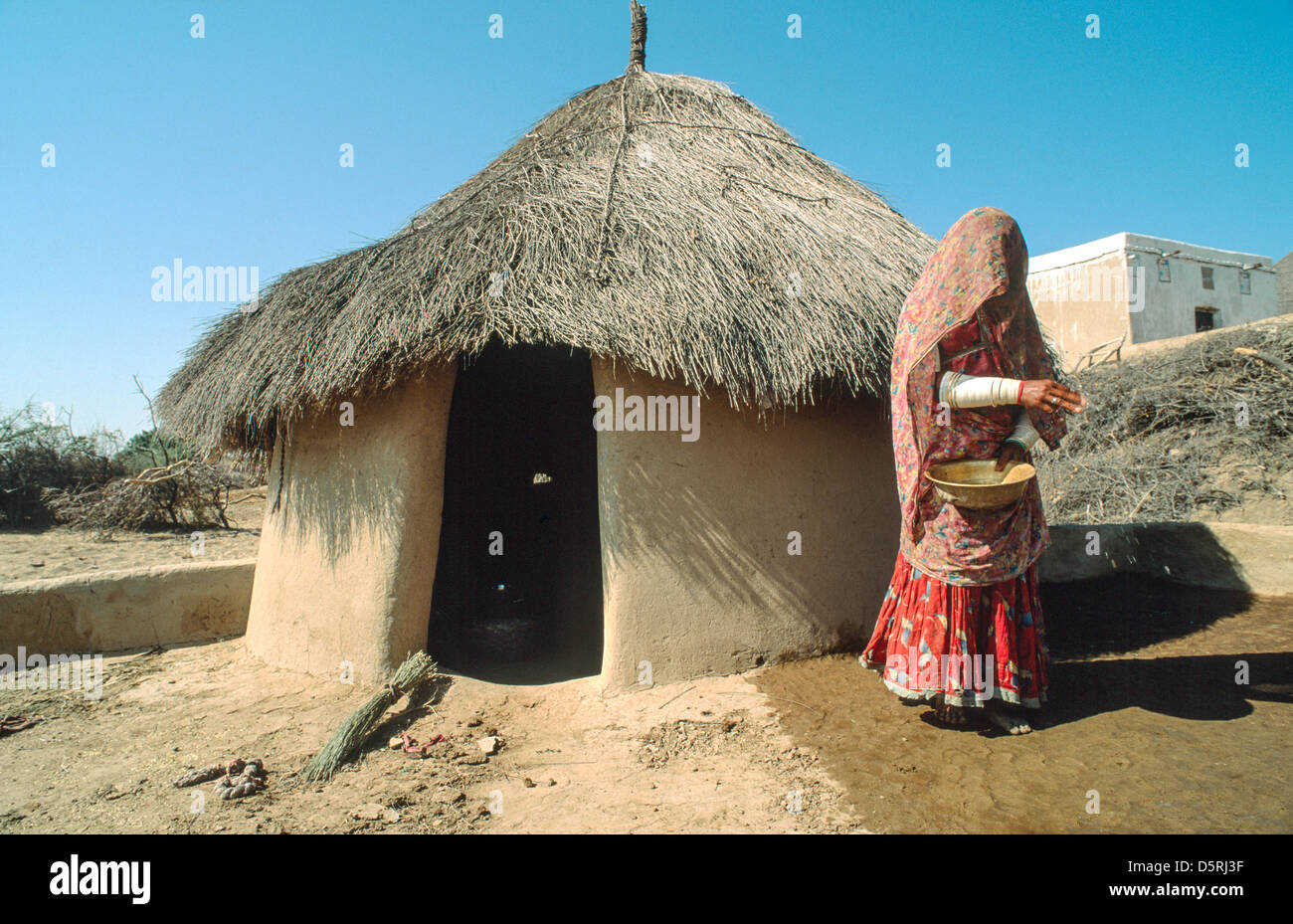 Woman dampening down the dust around her thatched mud hut. Islamkot ...