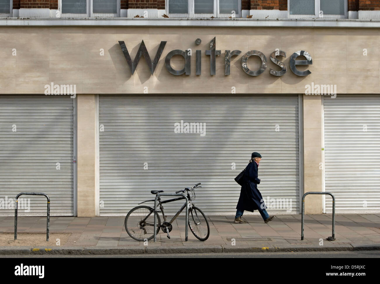 a woman walks past a closed branch of waitrose and a parked bike ...