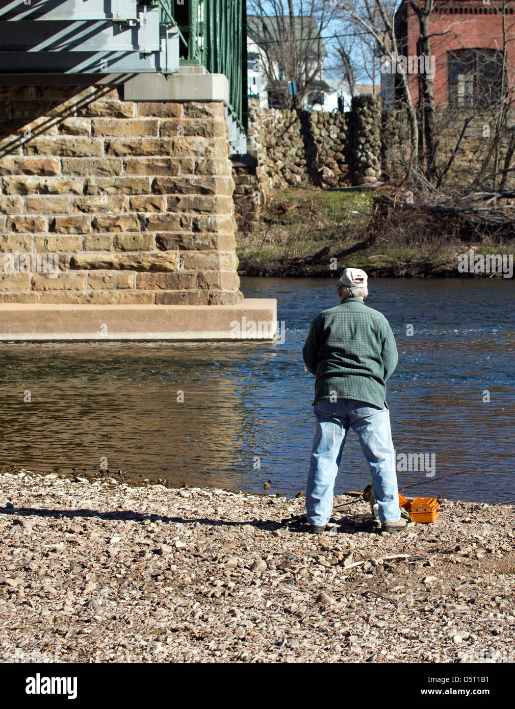Fisherman with tackle box fishing on the bank of a river under a bridge ...