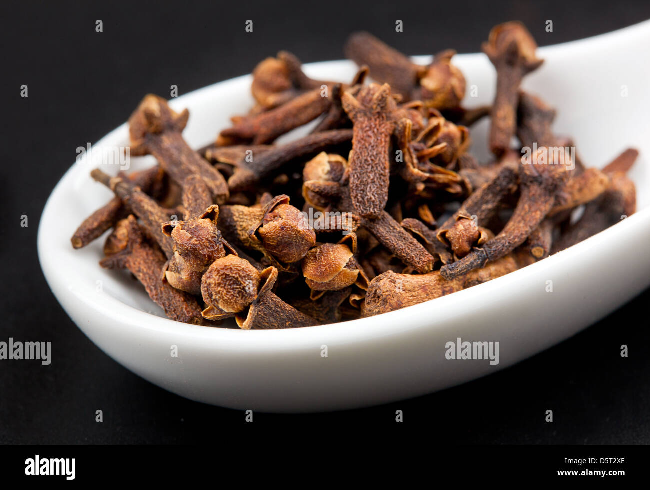 Cloves in the white spoon on black background Stock Photo - Alamy