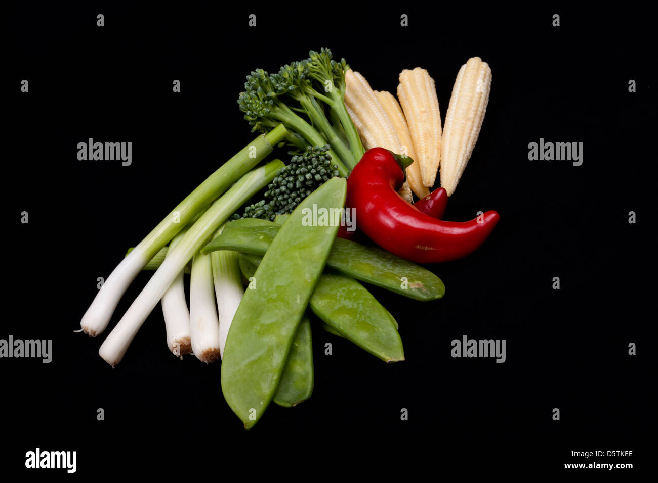 chilli, broccoli, baby leek, baby corn and mange tout on a black ...