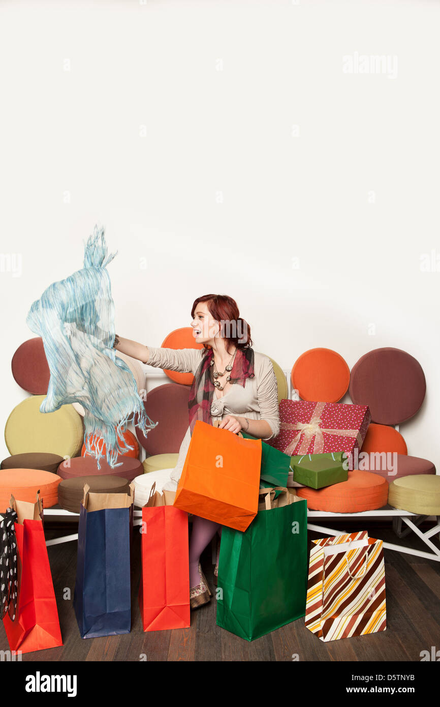 young woman pulling out a scarf from a shopping bag, sitting on a sofa ...