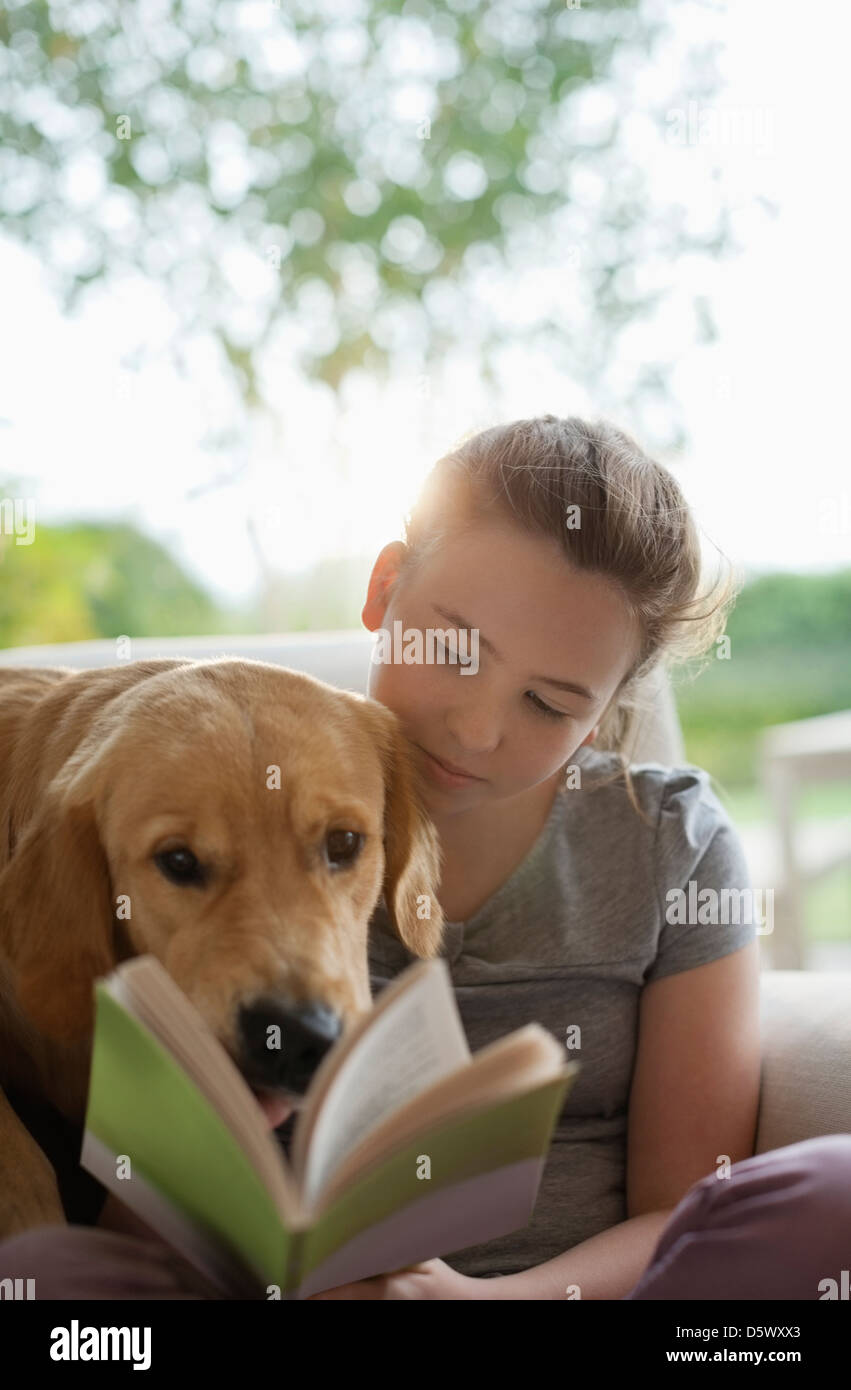 Girl reading with dog in armchair Stock Photo - Alamy