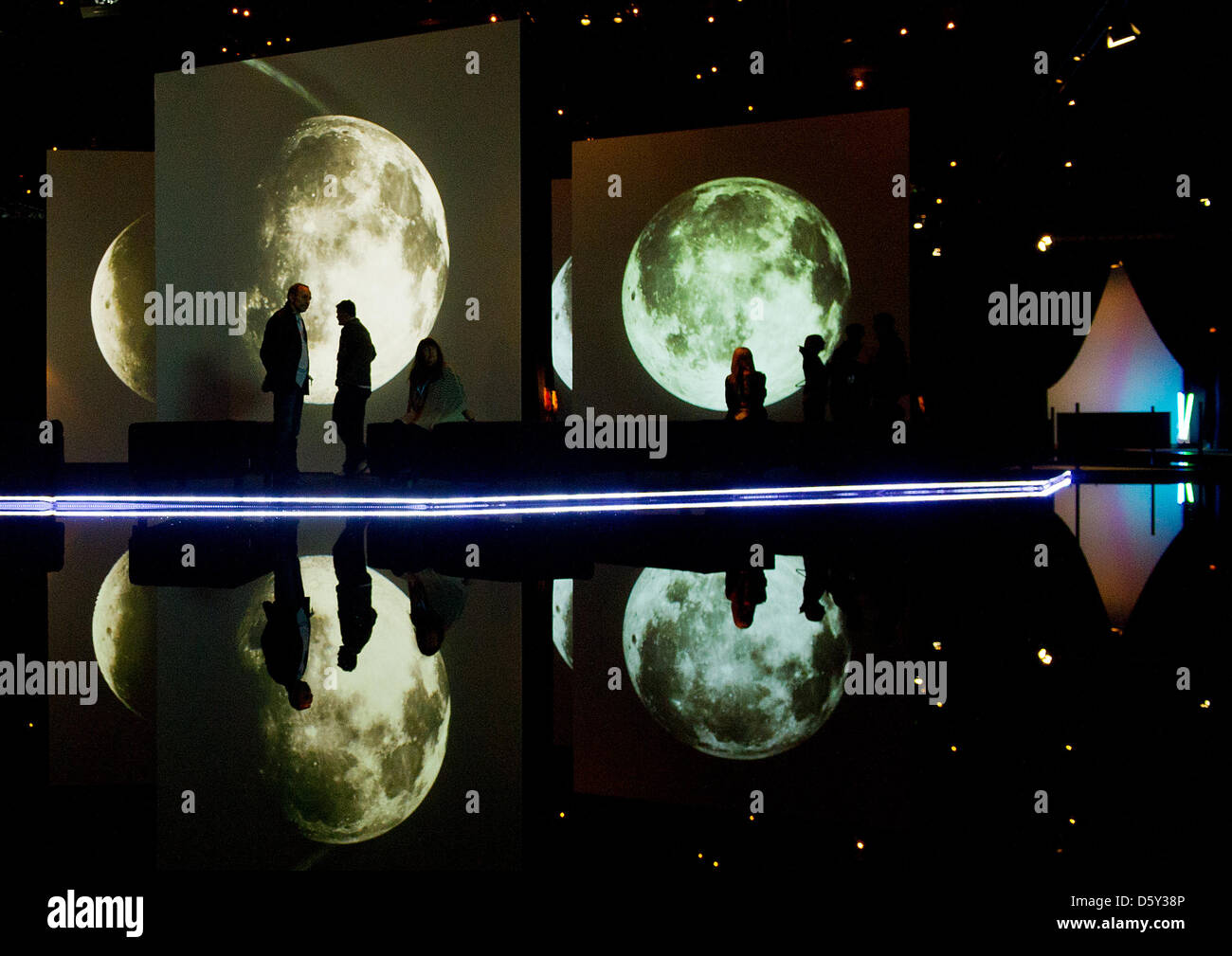 People stand in front of giant video screens showing the full moon ...