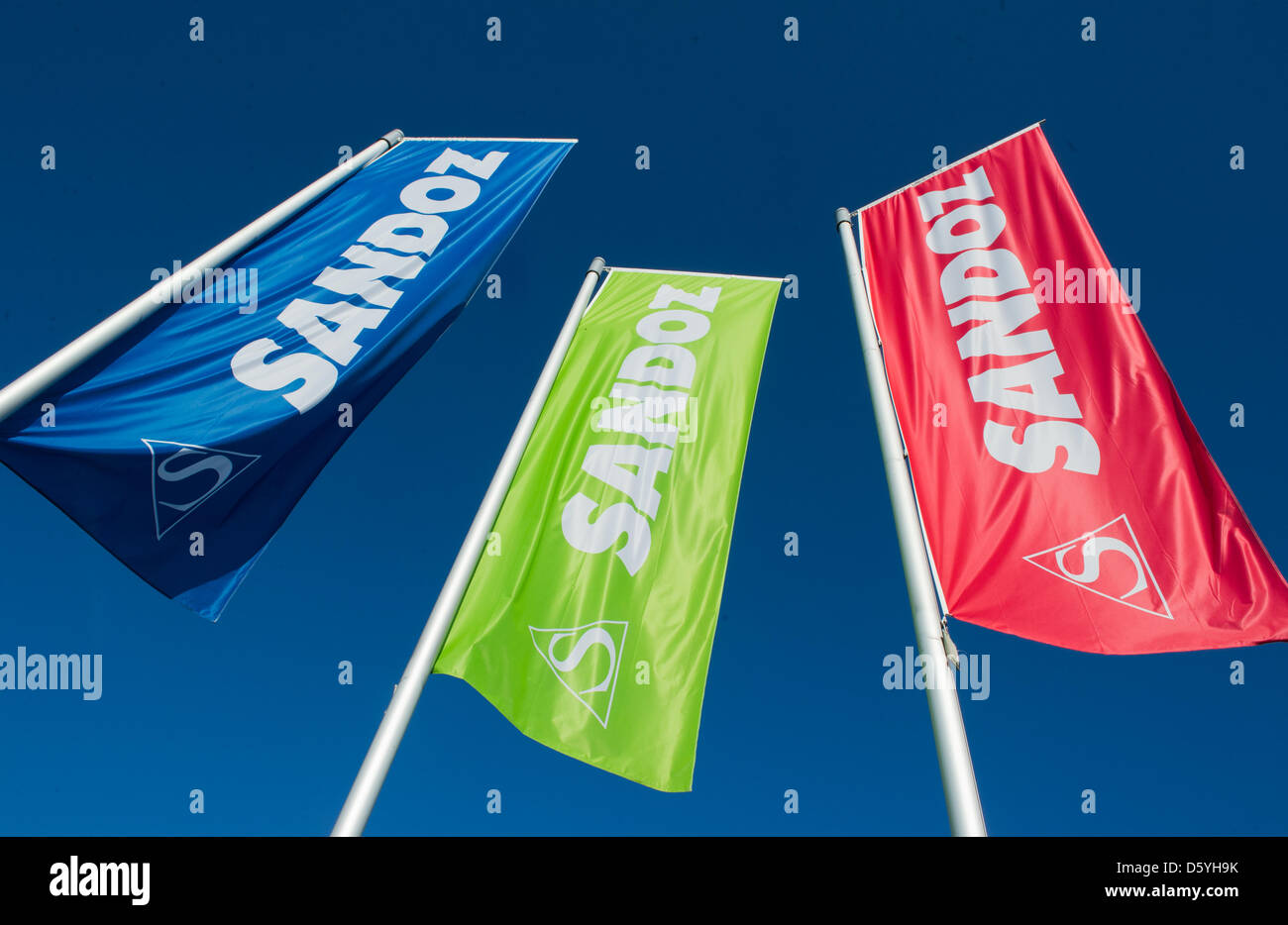 Three colorful flag with "Sandoz" written on them wave in front of a ...