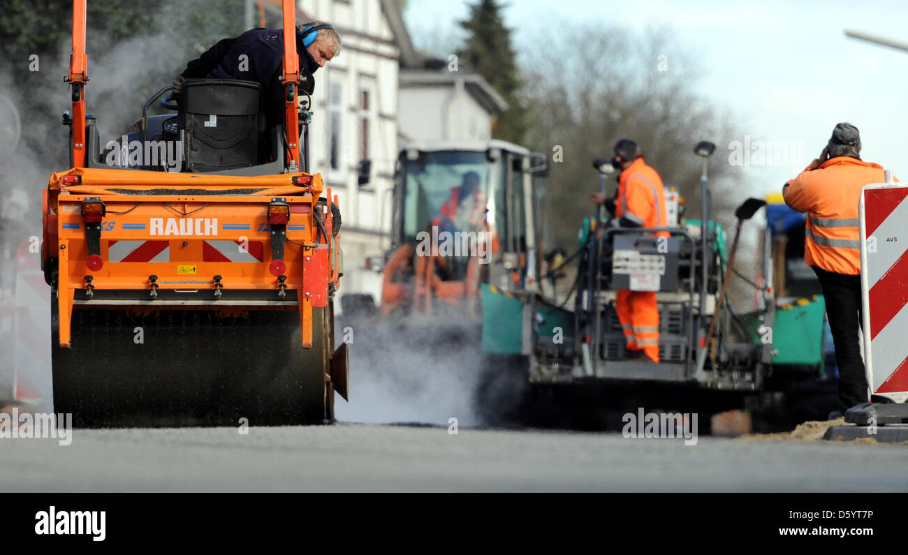 A roller steamrolls the fresh tarmac on street during construction work ...