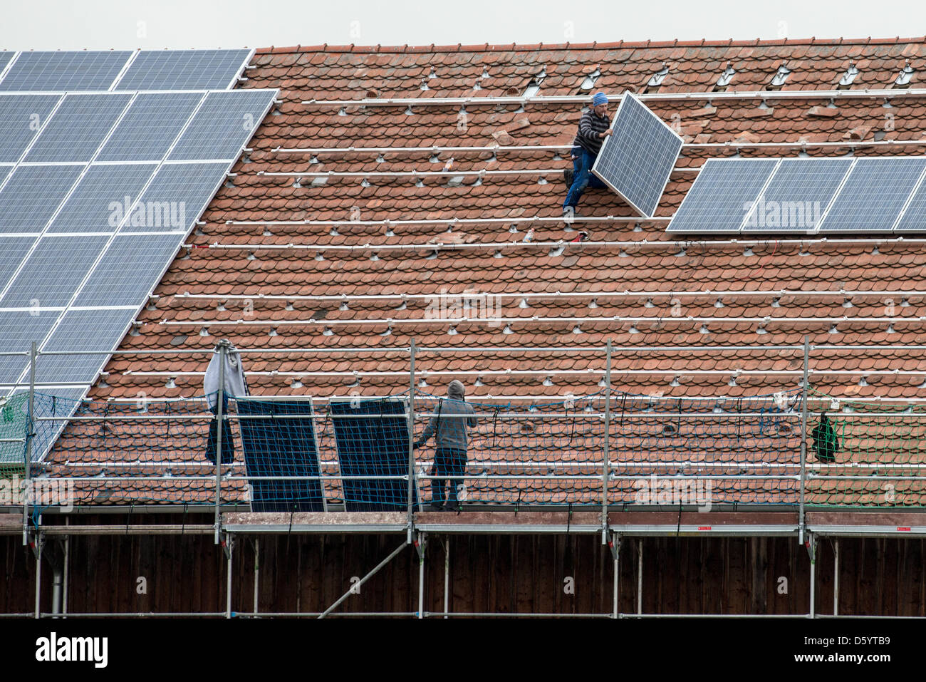 Workers install solar energy modules on a roof in Straubing, Germany ...