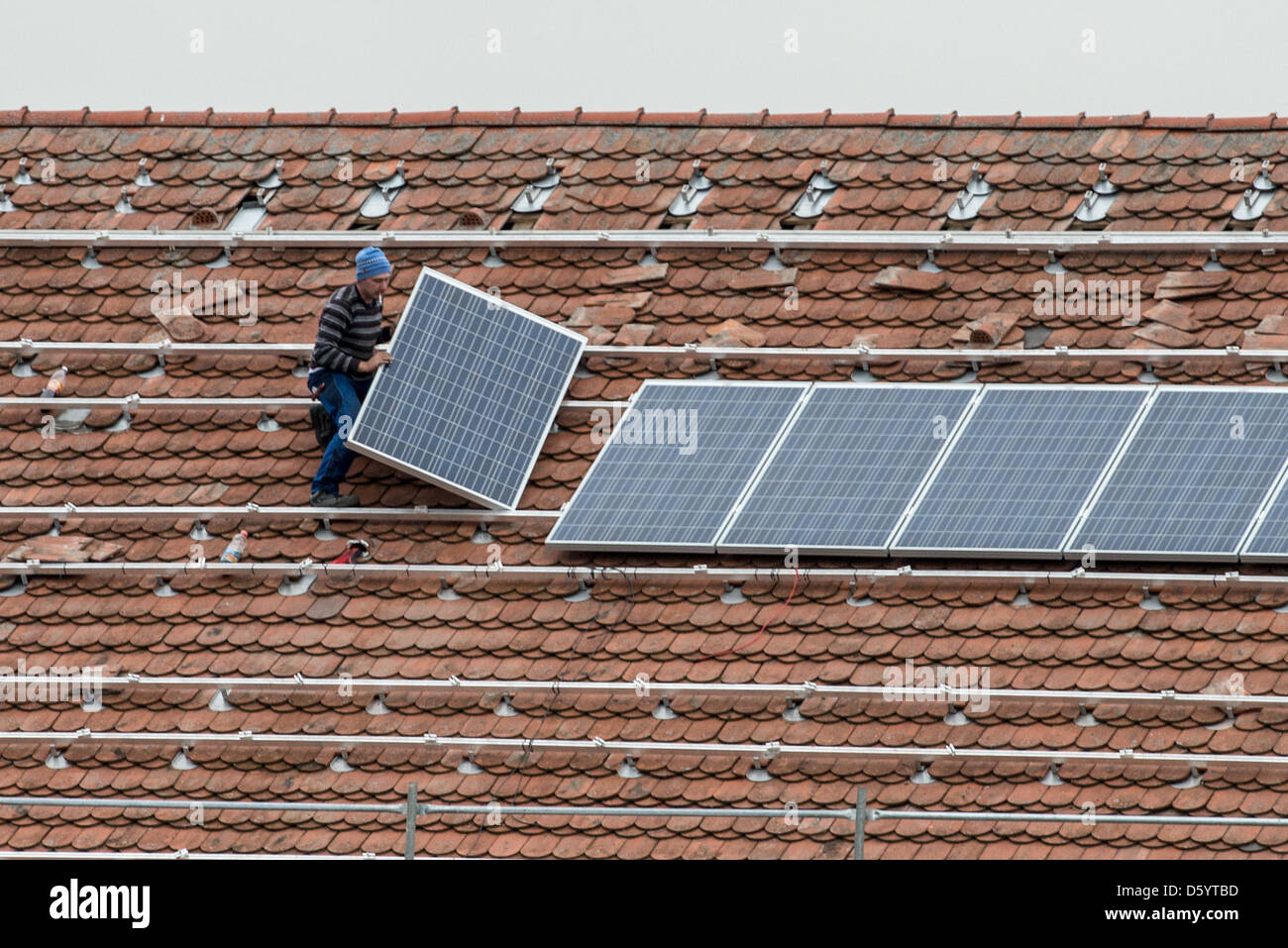 Workers install solar energy modules on a roof in Straubing, Germany ...