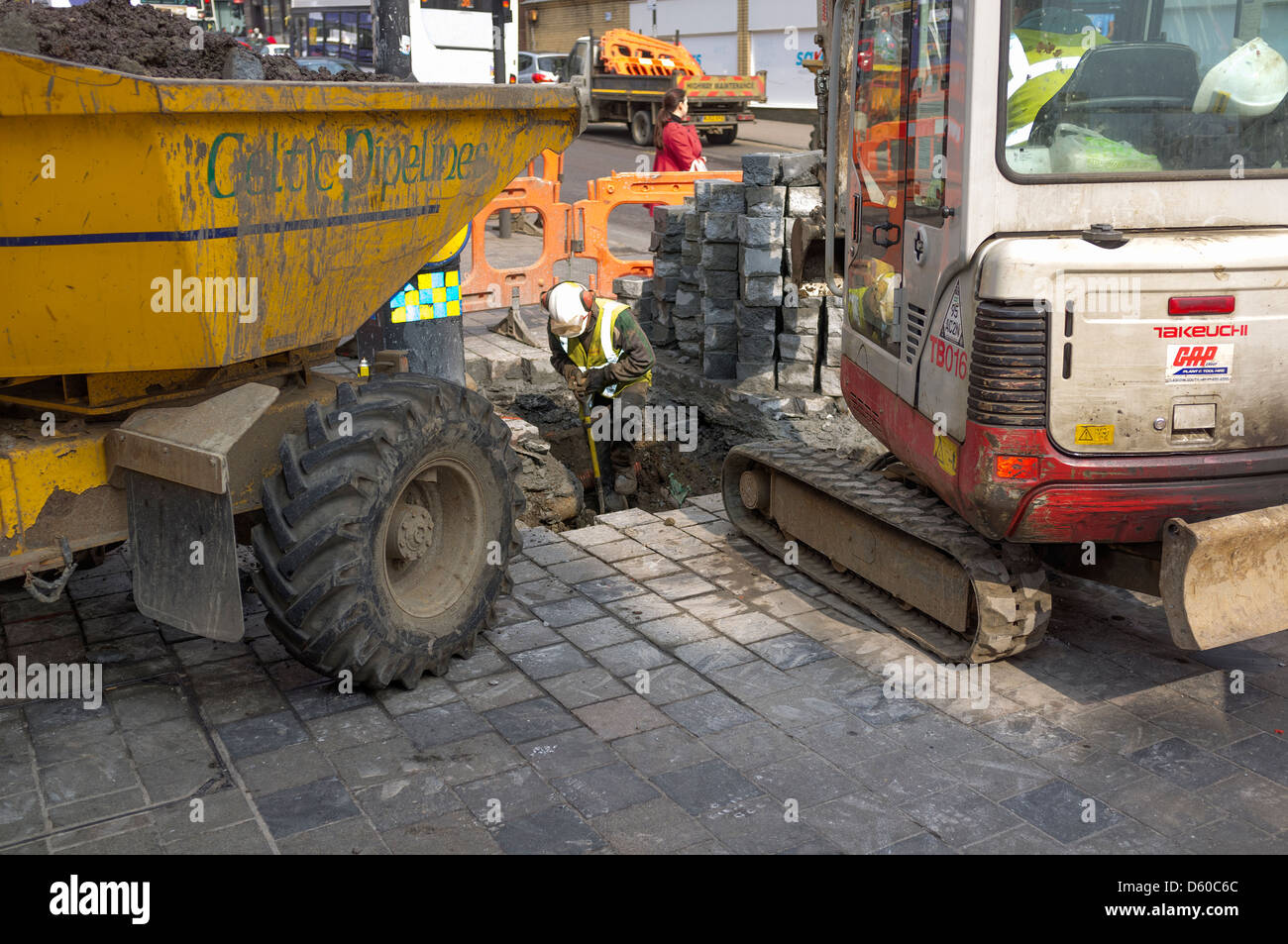 Workman digging a hole in a pavement using a shovel and a small JCB ...