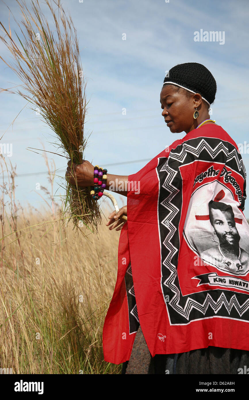 African woman wearing traditional dress tying a thatch bundle together ...