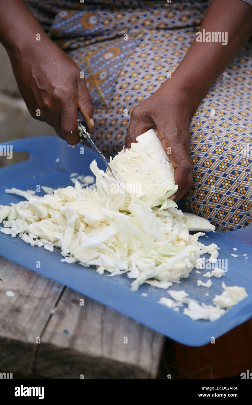 An African woman chops vegetables outside while her daughter looks on ...
