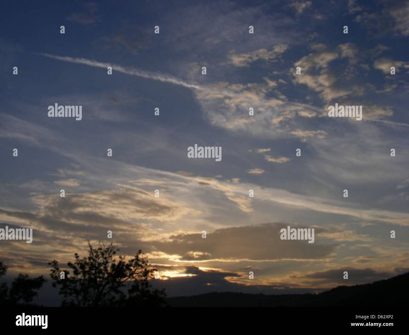 A dramatic sunrise sky with dark clouds and a fiery orange sun peeking through. The contrasting ...