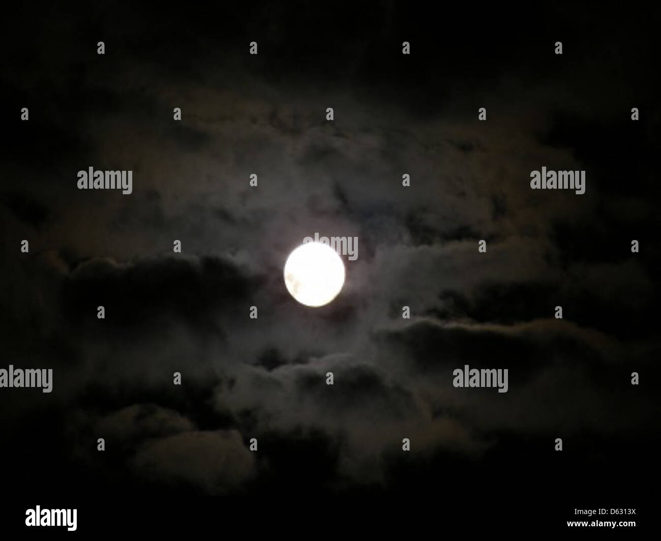 A dramatic image of the moon partially obscured by clouds, captured in ...