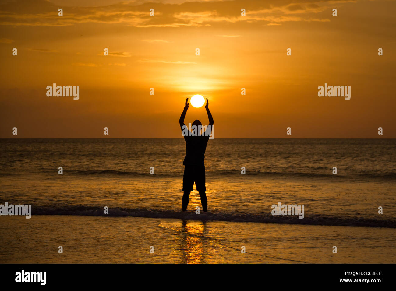 Silhoutted man on beach holding sun (sunset) between hands Stock Photo ...