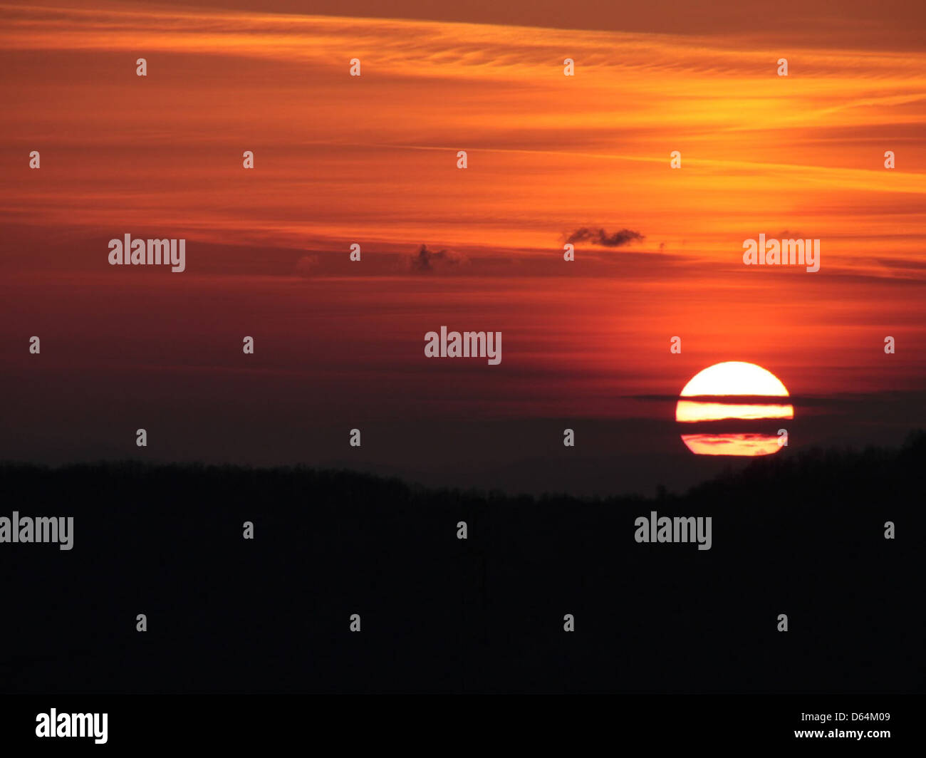 A striking dark red sunset, with the sun setting against a deep red sky ...