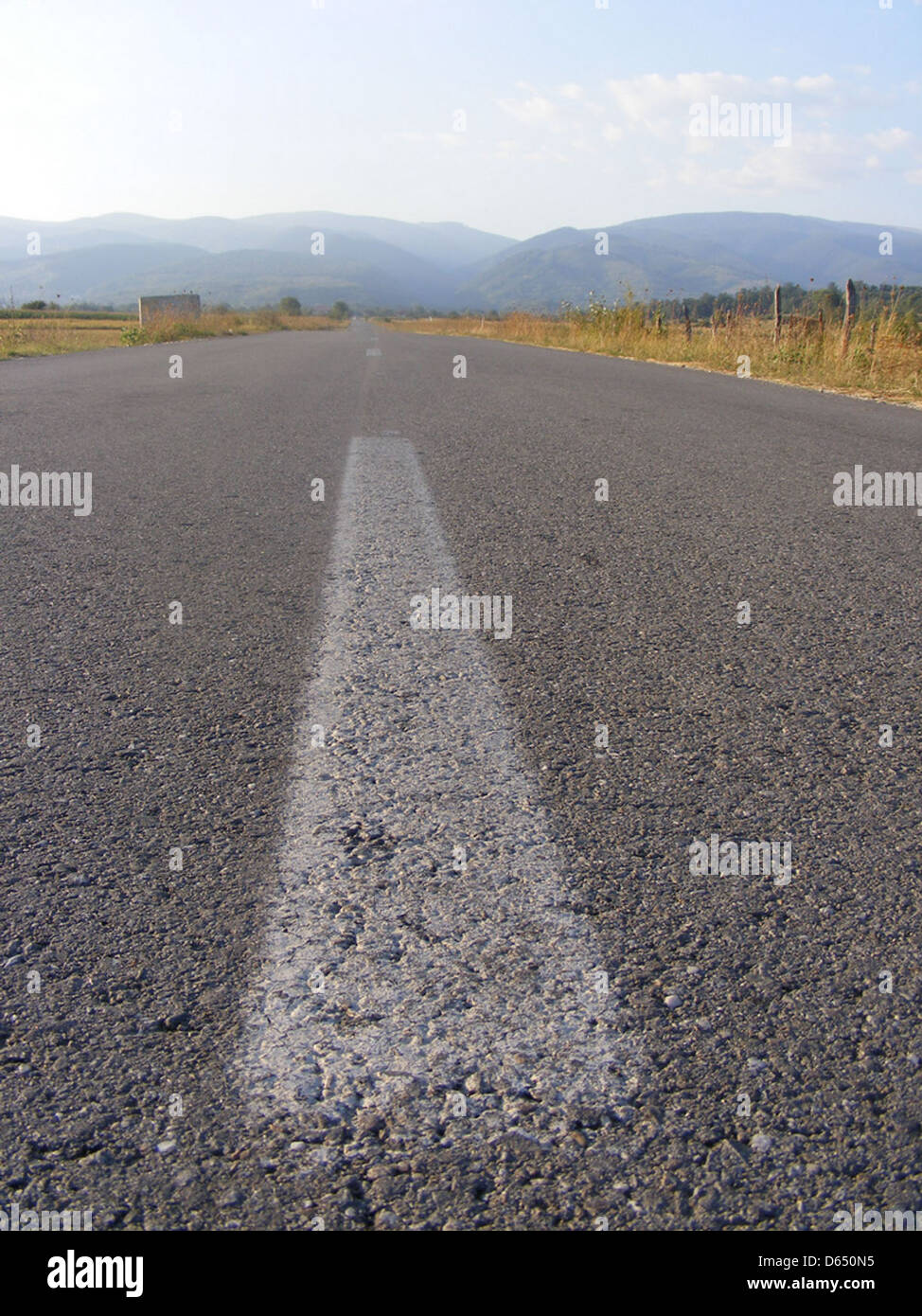 A long asphalt road stretching through a rural area, with open fields ...
