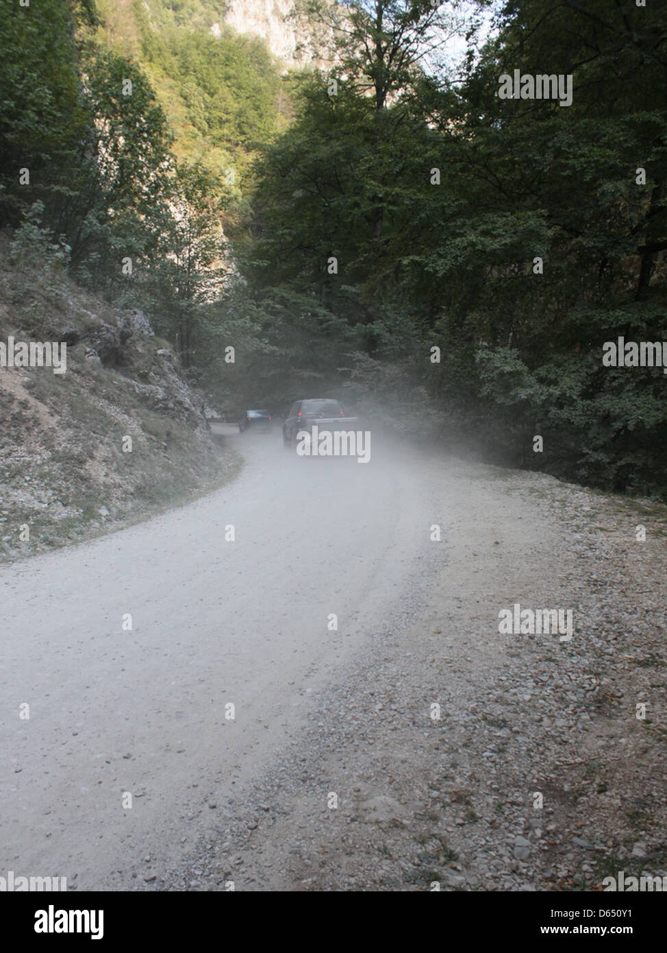 A car driving along a gravel road, leaving a dust trail behind. The ...