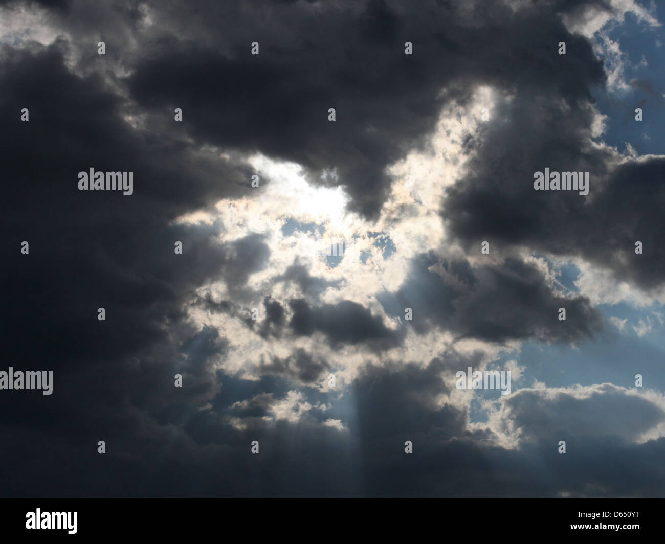 The image shows bright sun rays piercing through dark clouds during a ...