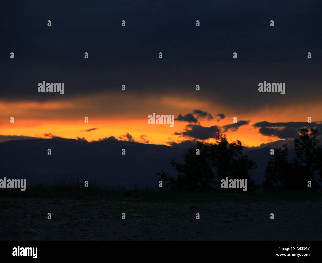 A dramatic sunset over a mountainous terrain, with storm clouds looming ...