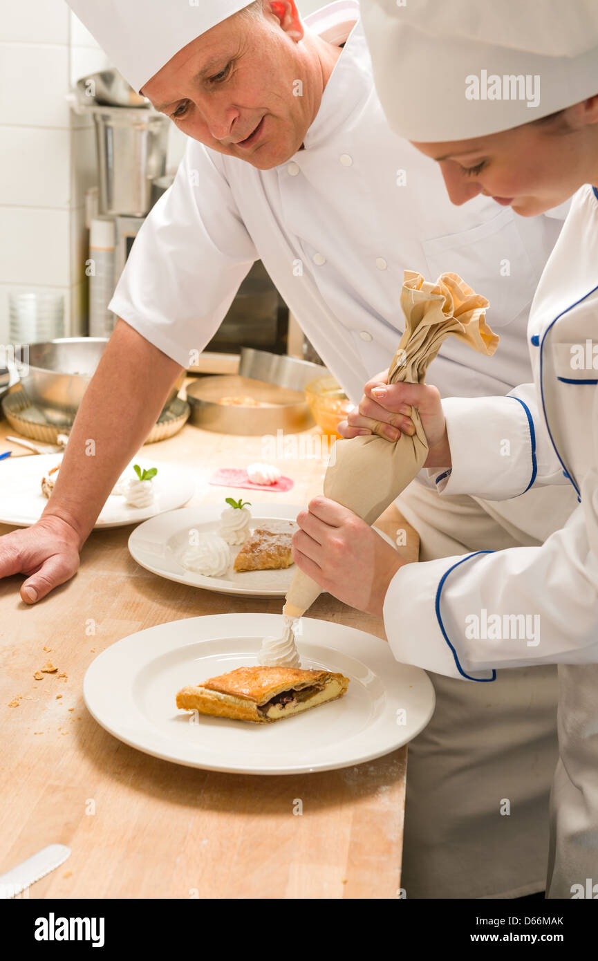 Female chef decorating cake with whipped cream using piping technique ...