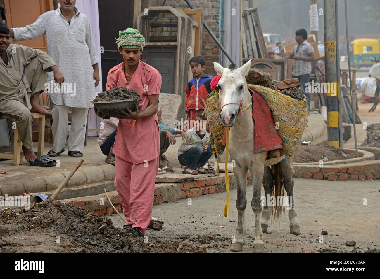A road worker shovelling up mud and old road tar in Old Delhi, India ...