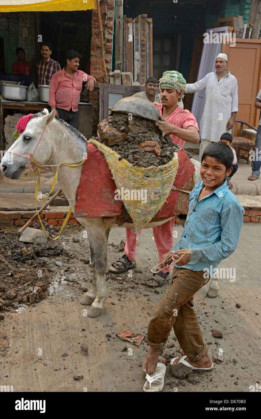 A road worker shovelling up mud and old road tar in Old Delhi, India ...