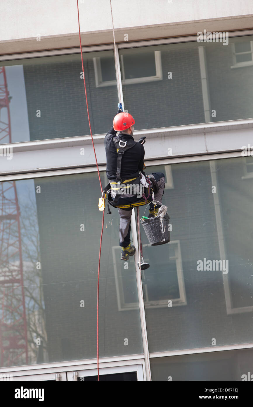 Commercial window cleaner wearing safety equipment cleaning a modern ...