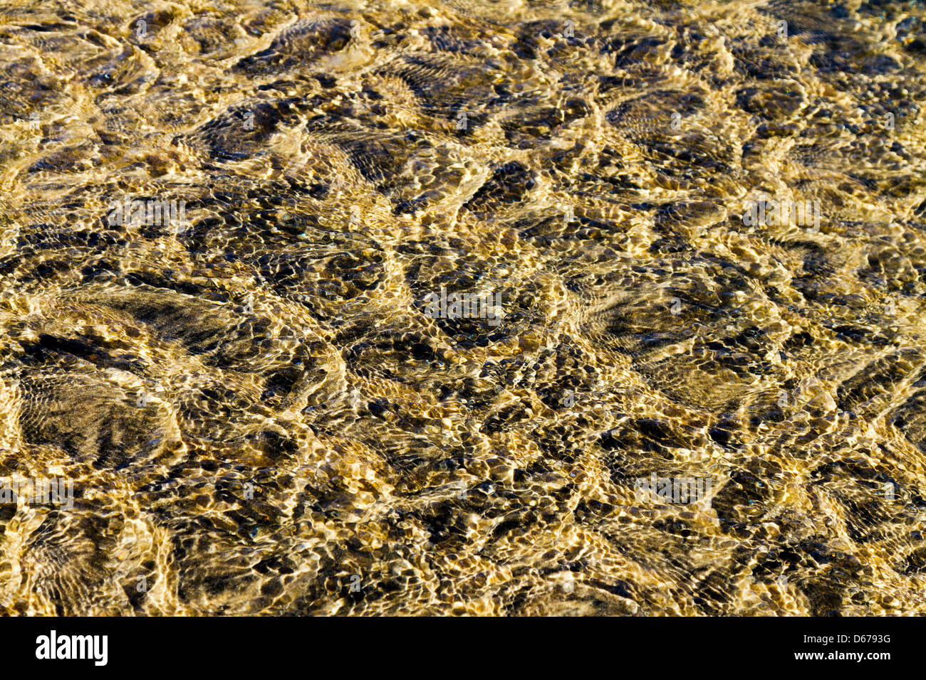 Water rippling over sand in a shallow creek bed forming artistic ...