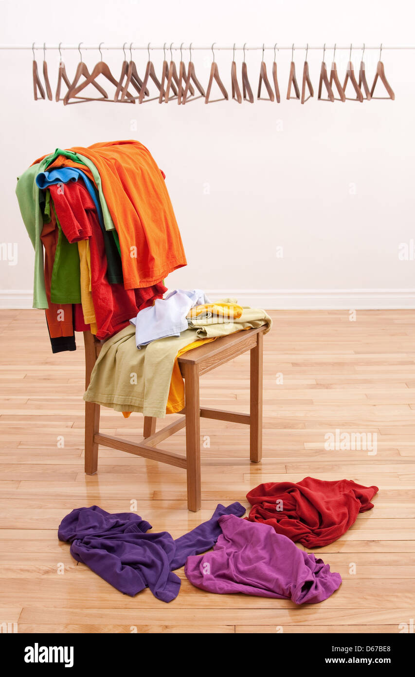 Colorful messy clothes on a chair and row of empty hangers on the ...