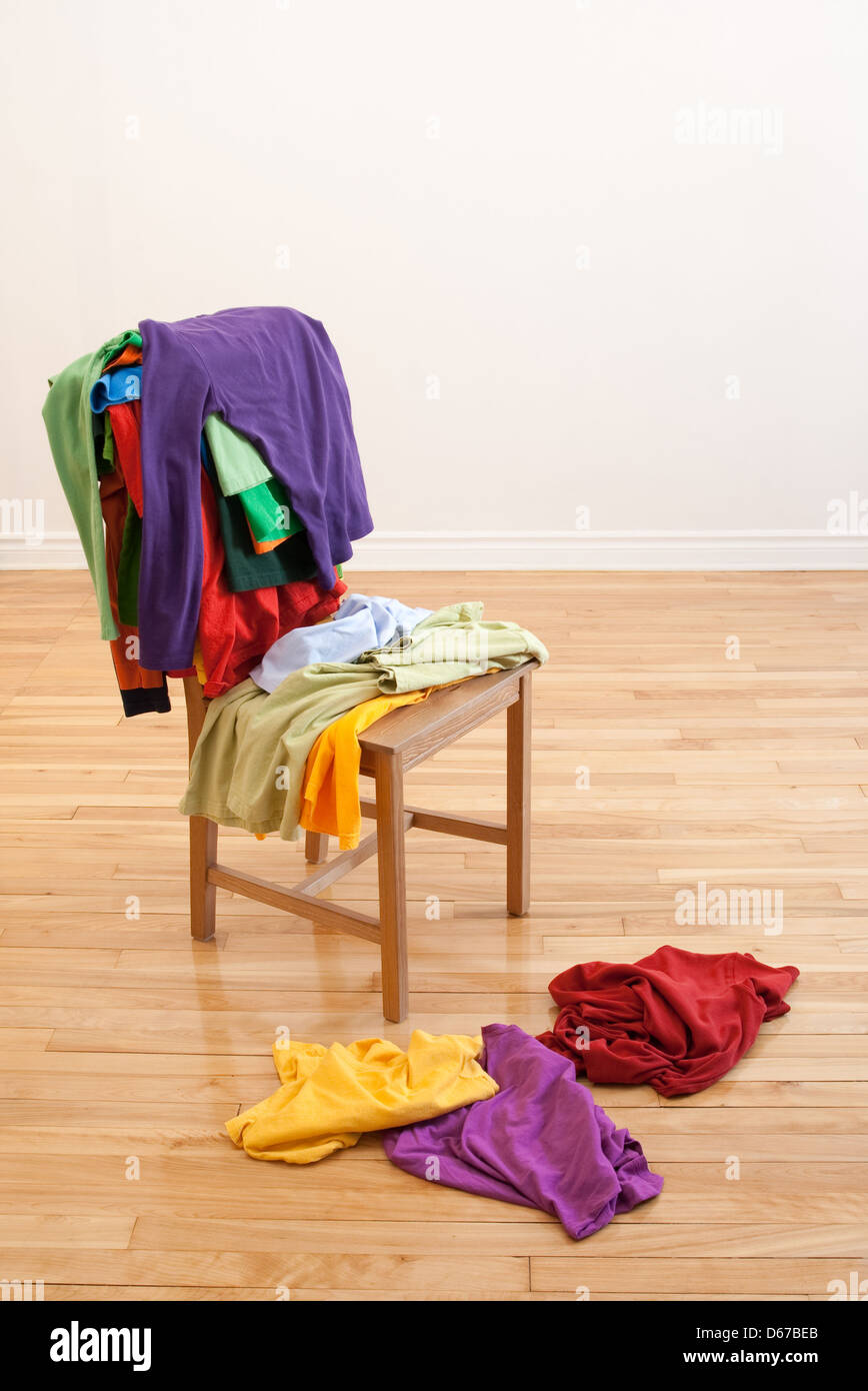 Lots of colorful messy clothes on a chair and on a wooden floor Stock ...