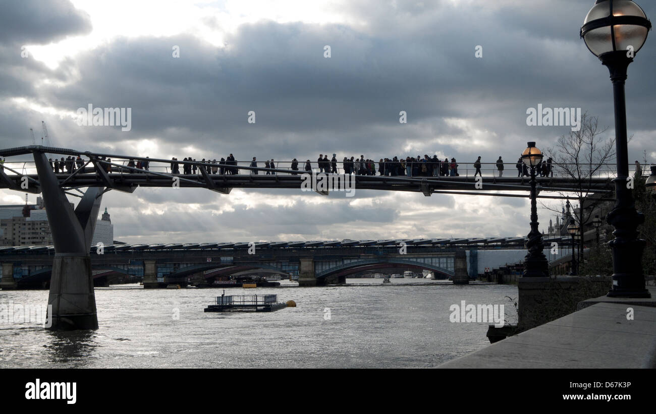 A side view of silhouetted pedestrians walking on the Millennium Bridge ...