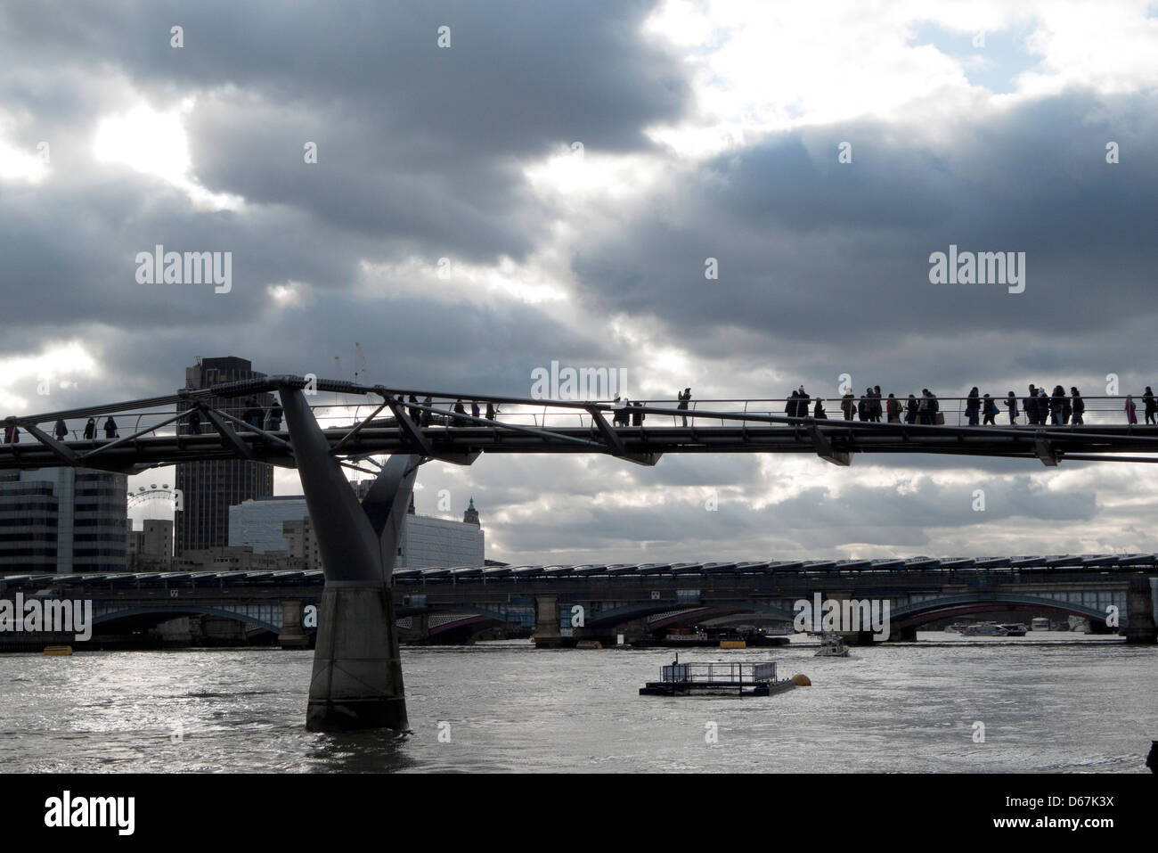 A side view of silhouetted pedestrians walking on the Millennium Bridge ...