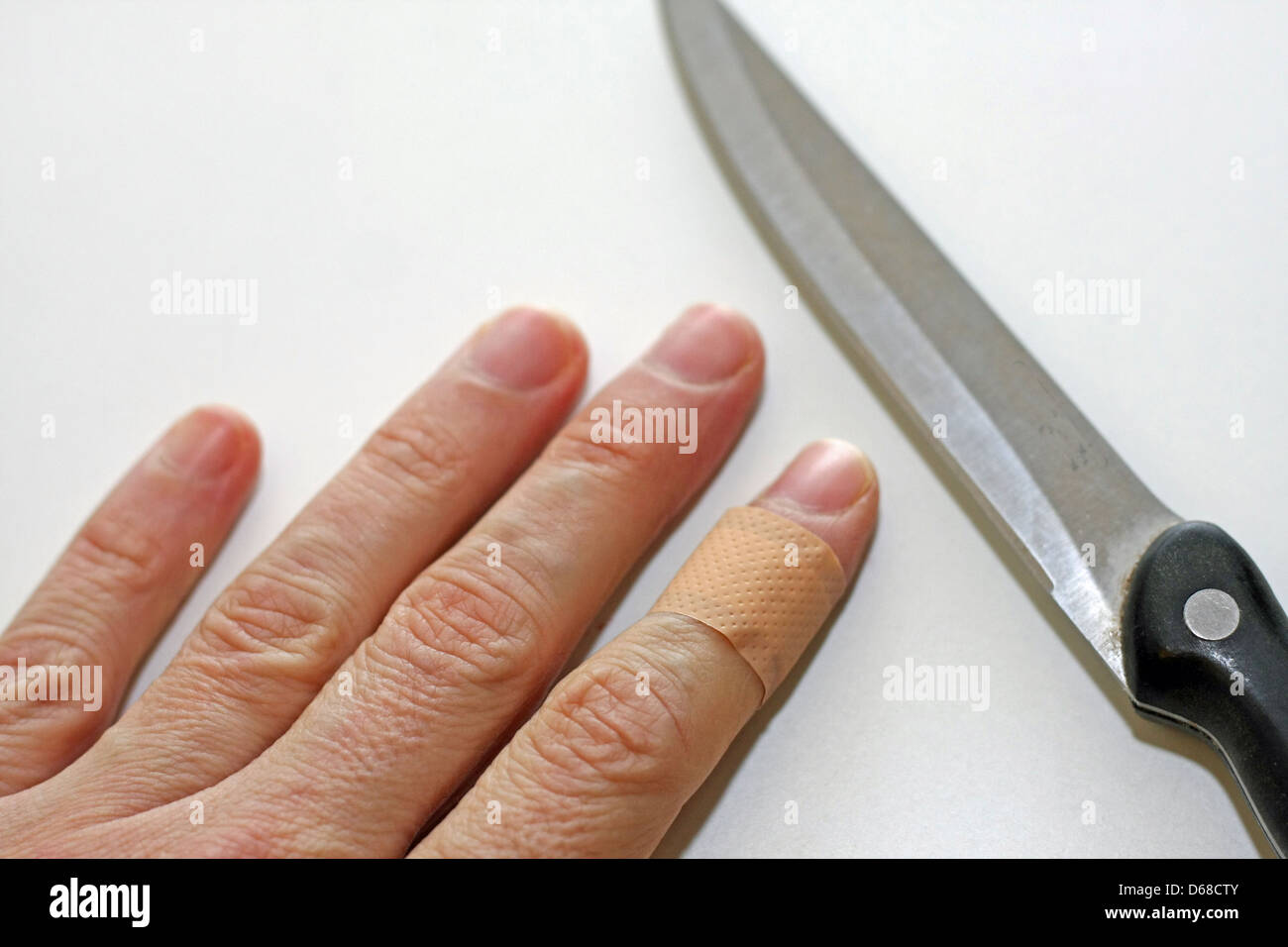 hand with finger with a band aid and the sharp blade of the knife in ...