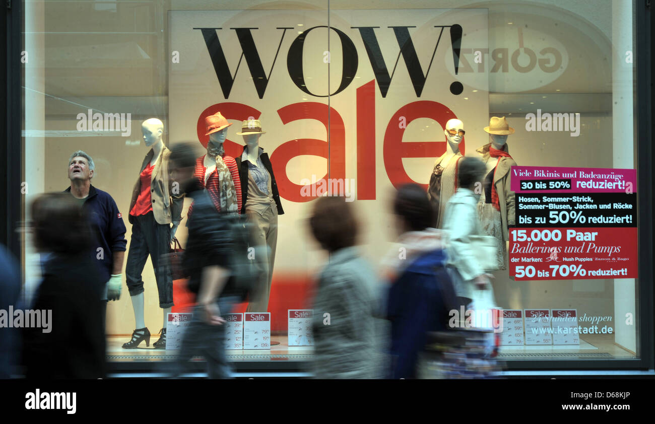 Pedestrians walk past a display window advertising reduced prices on ...